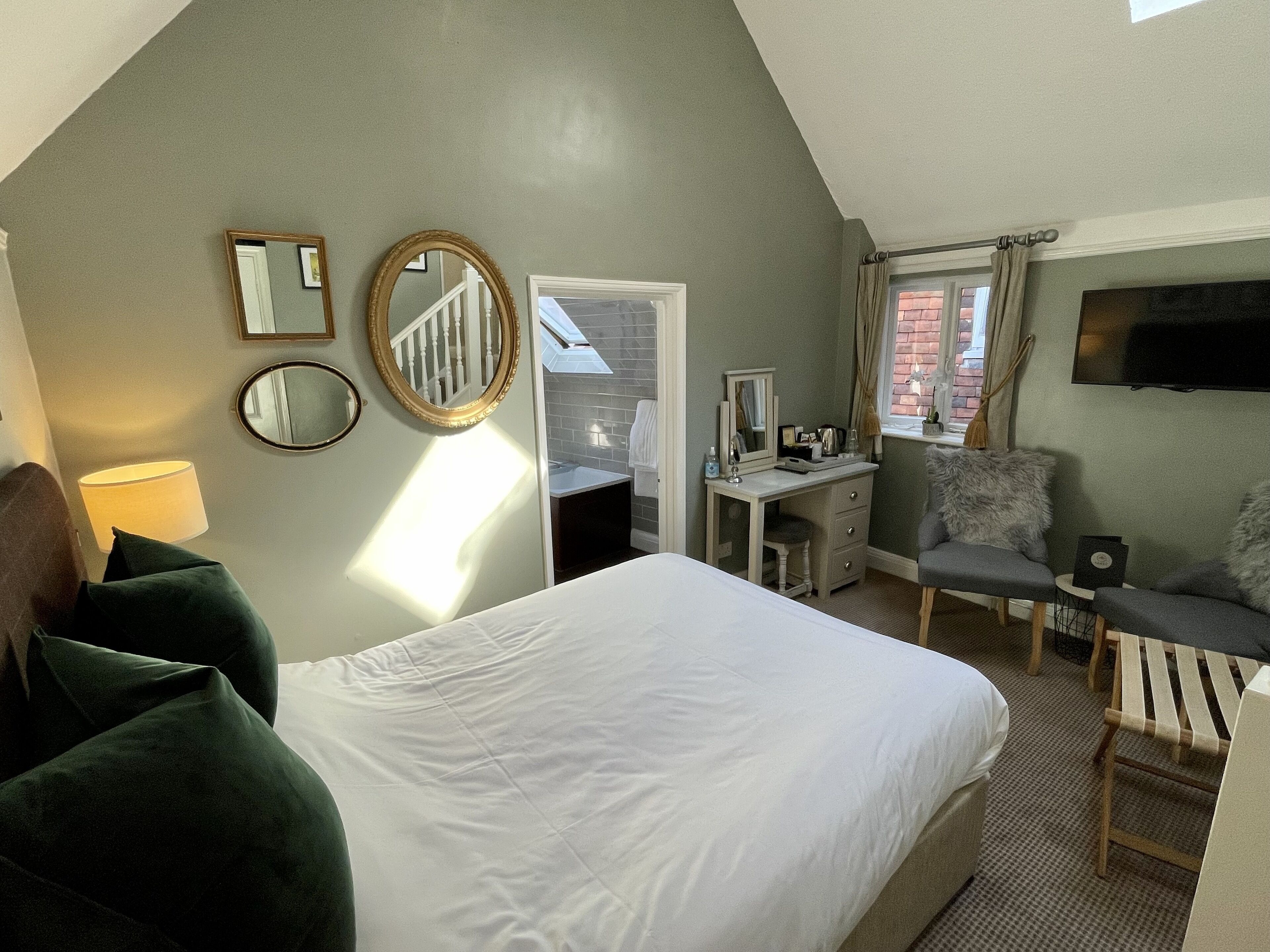 Quarto com cama, escrivaninha, cadeira, televisão e espelho.