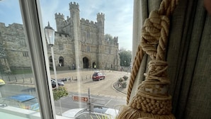 Vista de um castelo histórico através de uma janela, com uma decoração de corda pendurada na cortina.