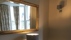 Um quarto com um armário de madeira, uma luminária, uma cadeira, um espelho e um vaso com flores.