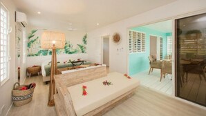 Quarto com cama, uma mesinha, luminária de chão e vista para uma sala de jantar.