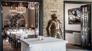 Uma sala de jantar com uma mesa comprida posta para refeição, um candelabro e uma estátua de cavaleiro.