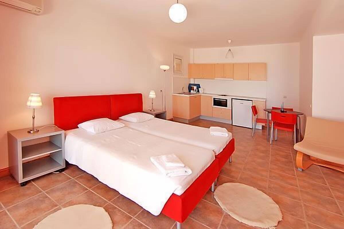 Quarto de hotel com uma cama grande, uma mesa e uma cozinha compacta.
