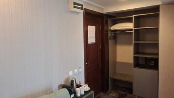 Quarto de hotel com sofá, uma mesinha com chaleira e chávenas, um armário com prateleiras e um tapete estampado.