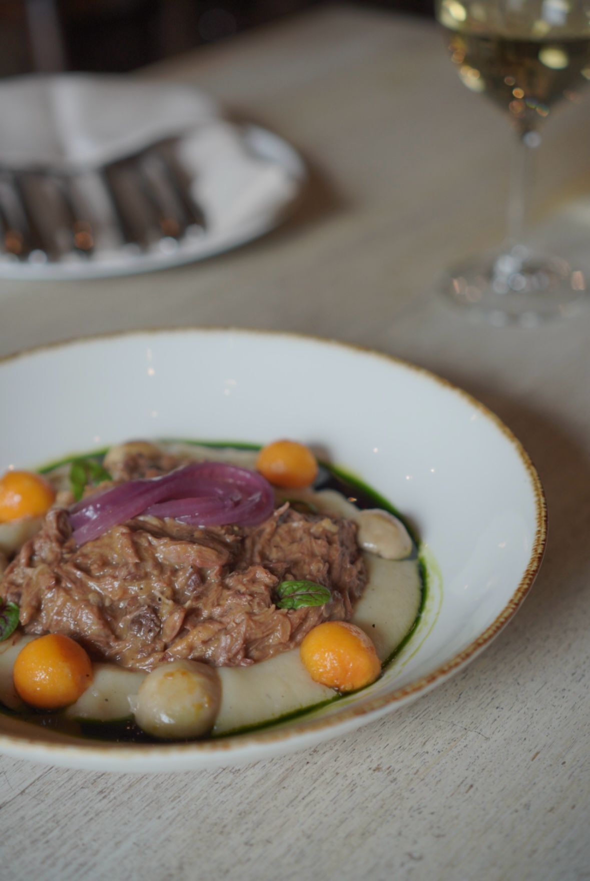 Prato de comida com carne, legumes e pequenas esferas, possivelmente azeitonas, sobre um prato branco com borda verde.