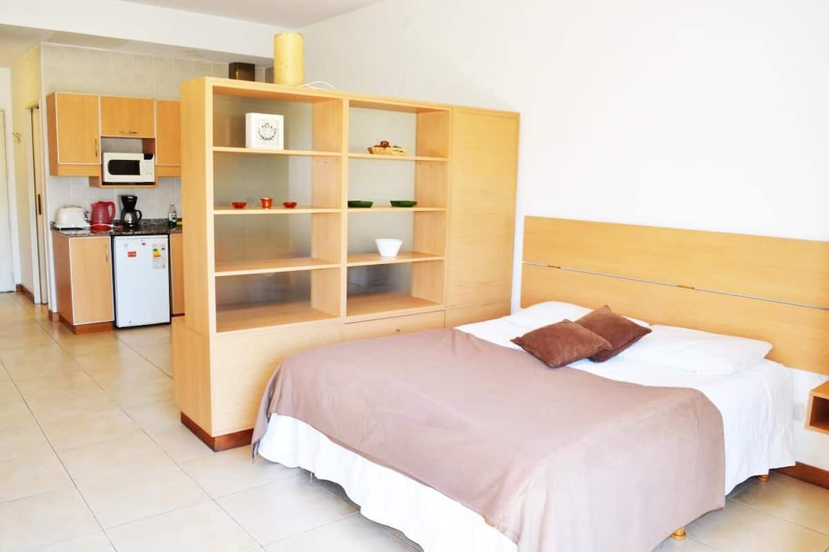 Quarto de hotel com cama, guarda-roupa de madeira, cozinha compacta com micro-ondas e frigorífico.