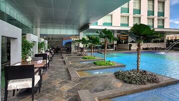 Área de piscina de hotel com espaço para sentar ao ar livre e um edifício moderno ao fundo.