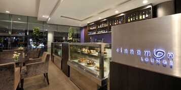 Uma área de estar moderna com uma vitrine de sobremesas, um bar com diversos tipos de bebidas e uma placa com a inscrição 'cinnamon lounge'.