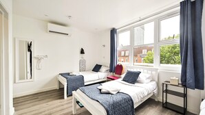 Quarto moderno com duas camas, uma janela com cortinas, uma mesinha de cabeceira e um ar condicionado.