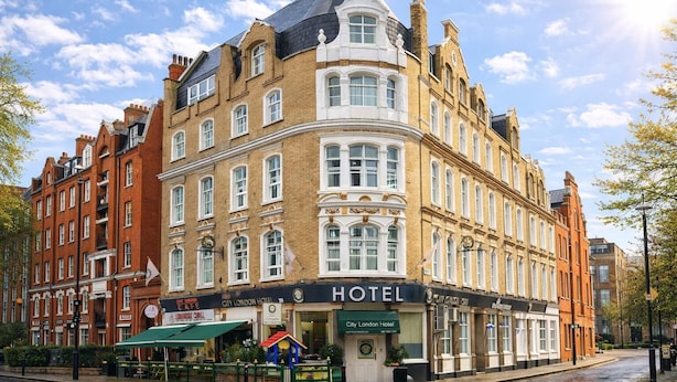Um edifício de esquina com uma placa que diz "HOTEL", apresentando arquitetura clássica com várias janelas e uma torre de canto imponente.