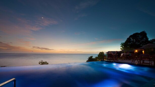 Uma piscina infinita com vista para o mar ao entardecer.