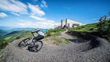 Ciclista de montanha em trilha de cascalho, com um edifício moderno ao fundo.