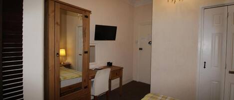 Quarto com cama, penteadeira de madeira, escrivaninha, cadeira, televisão e lustre.