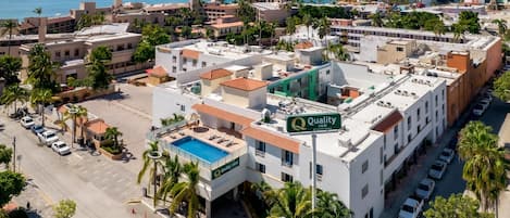 Um hotel com piscina no terraço, rodeado por palmeiras e vista para o oceano.