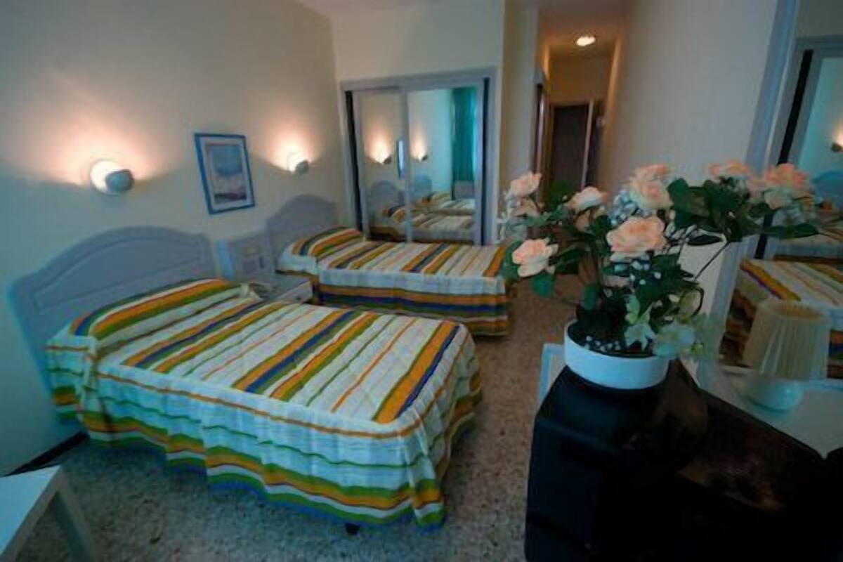 Quarto de hotel com duas camas, um espelho e um vaso com flores.