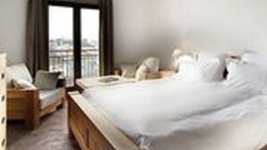 Quarto de hotel com uma cama grande, uma escrivaninha, uma cadeira e vista da cidade através de uma janela ampla.