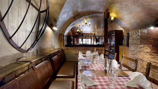 Restaurante com paredes de pedra, bancos de madeira e toalha de mesa xadrez.
