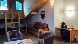 Quarto estilo loft acolhedor, com vigas de madeira aparentes, cama no mezanino, escrivaninha e sofá.