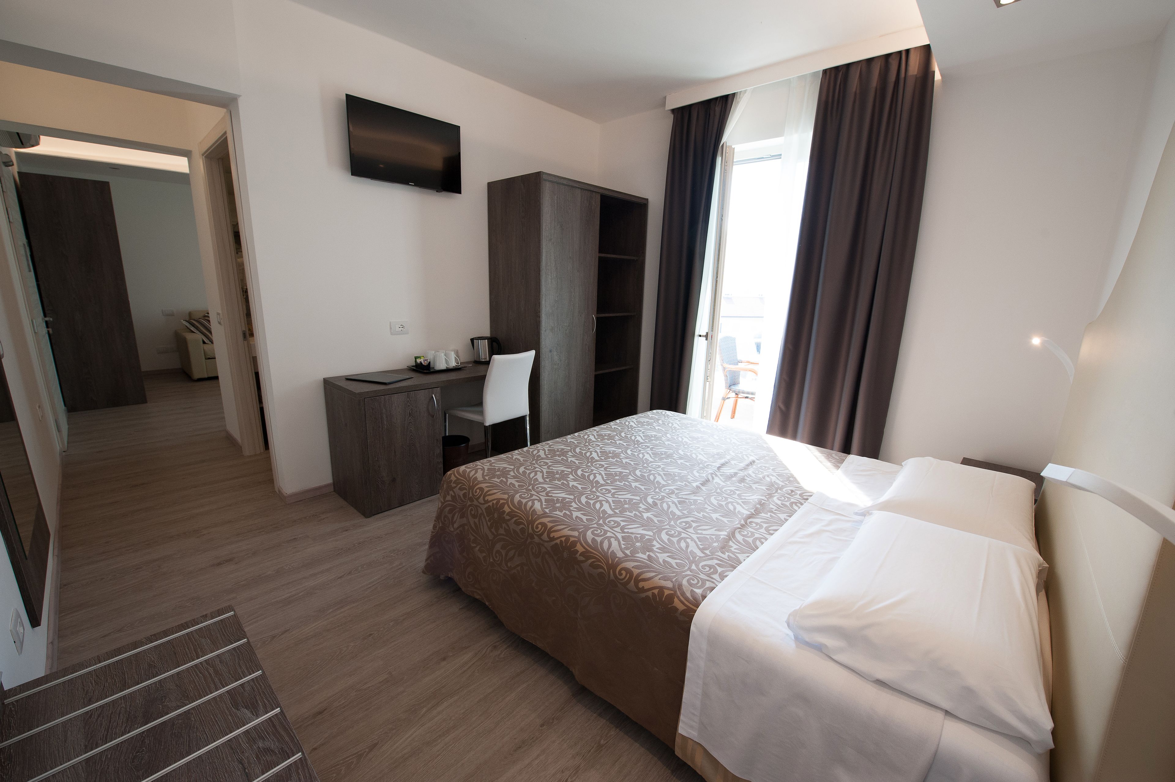 Quarto de hotel com cama, escrivaninha, armário e televisão na parede.