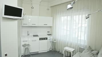 Cozinha moderna com eletrodomésticos brancos, televisão integrada e área de jantar com mesa e dois banquetes.