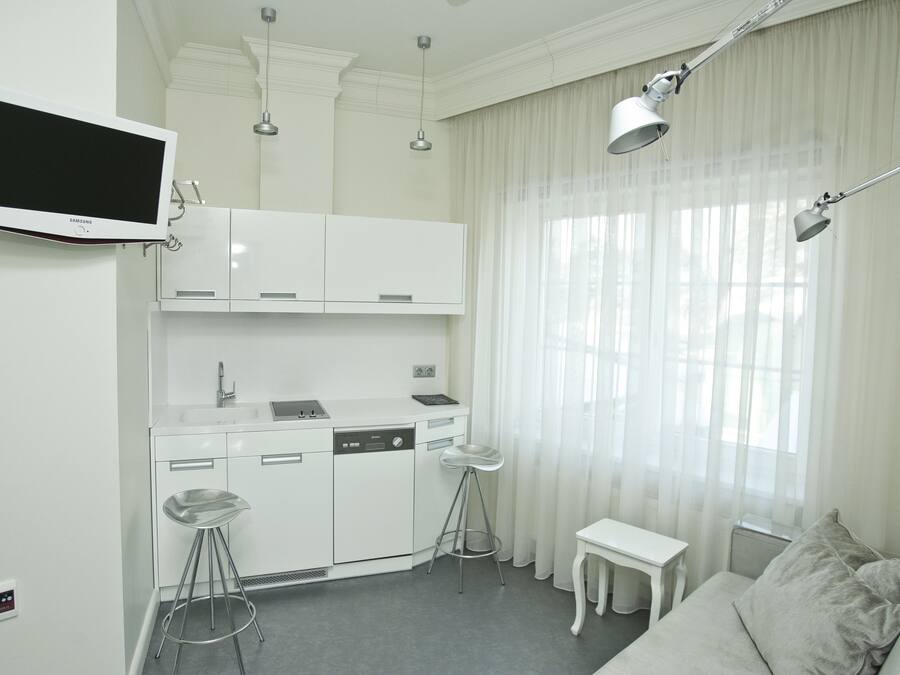 Cozinha moderna com eletrodomésticos brancos, televisão integrada e área de jantar com mesa e dois banquetes.
