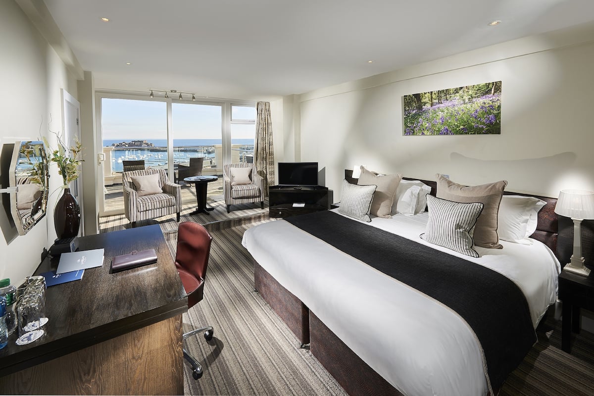 Quarto de hotel com uma cama grande, uma mesa de escritório com um laptop, uma TV e vista para o mar.