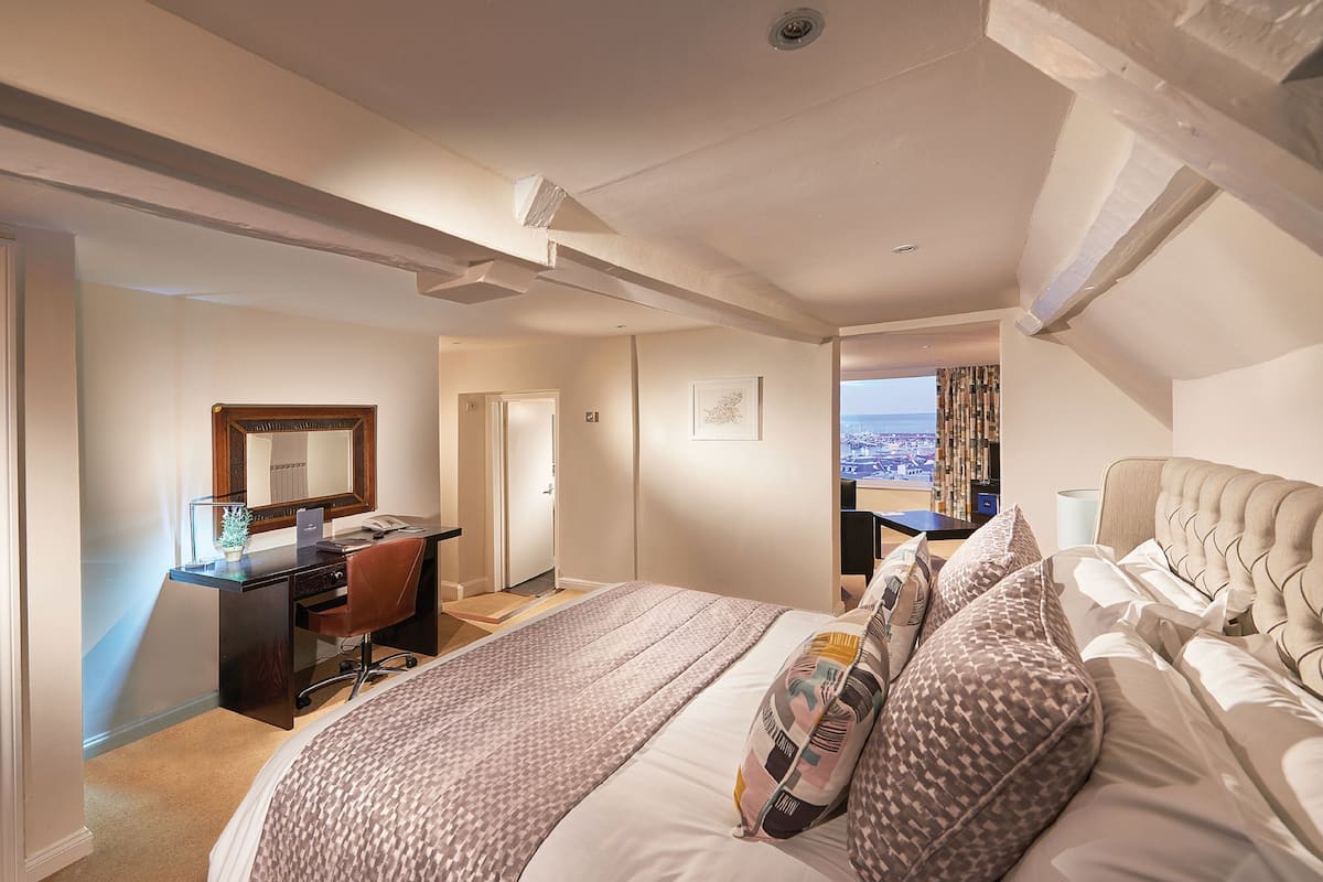 Quarto de hotel com uma cama grande, uma escrivaninha com cadeira, um espelho e vista da cidade.