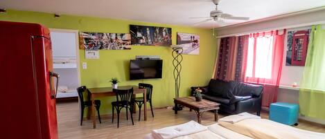 Um espaço compacto com cama, sofá, mesa de jantar com cadeiras, televisão e frigorífico vermelho.