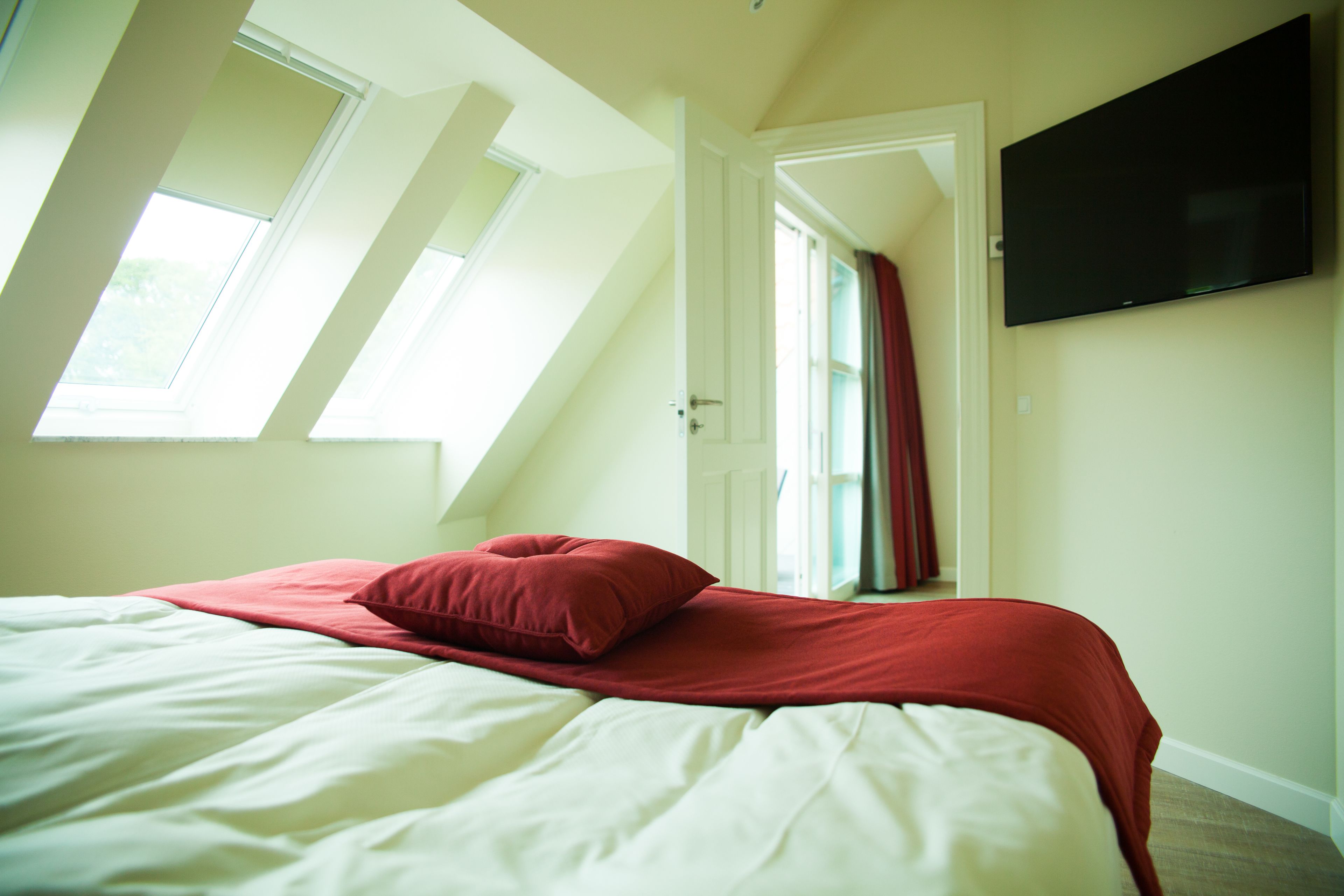 Quarto com cama, televisão montada na parede e claraboias.
