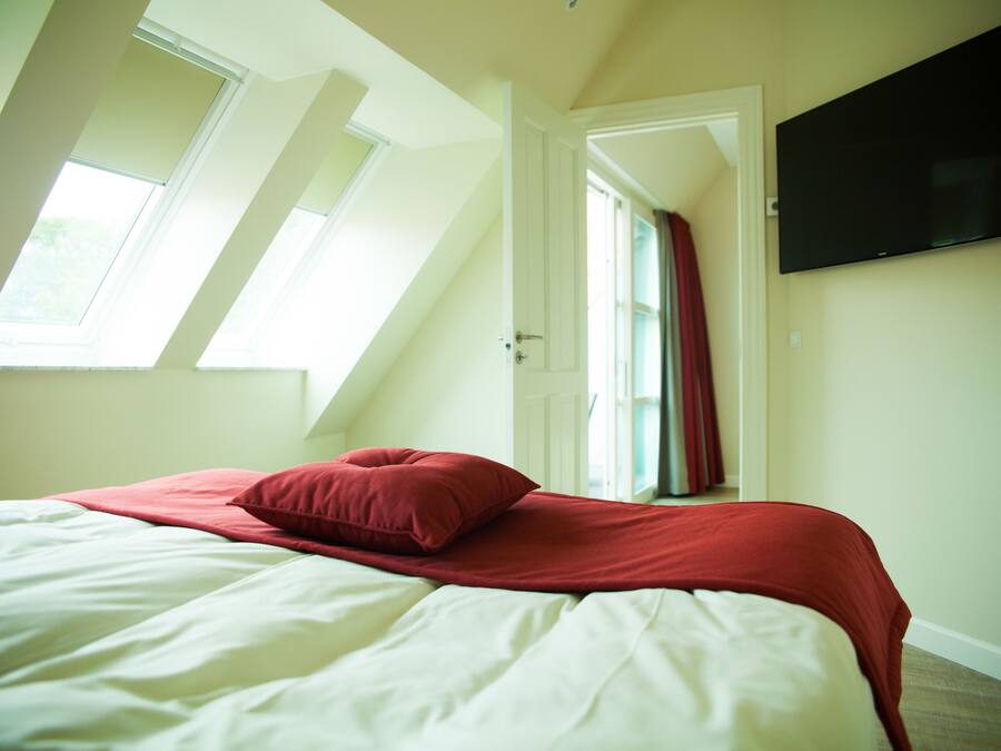 Quarto com cama, televisão montada na parede e claraboias.