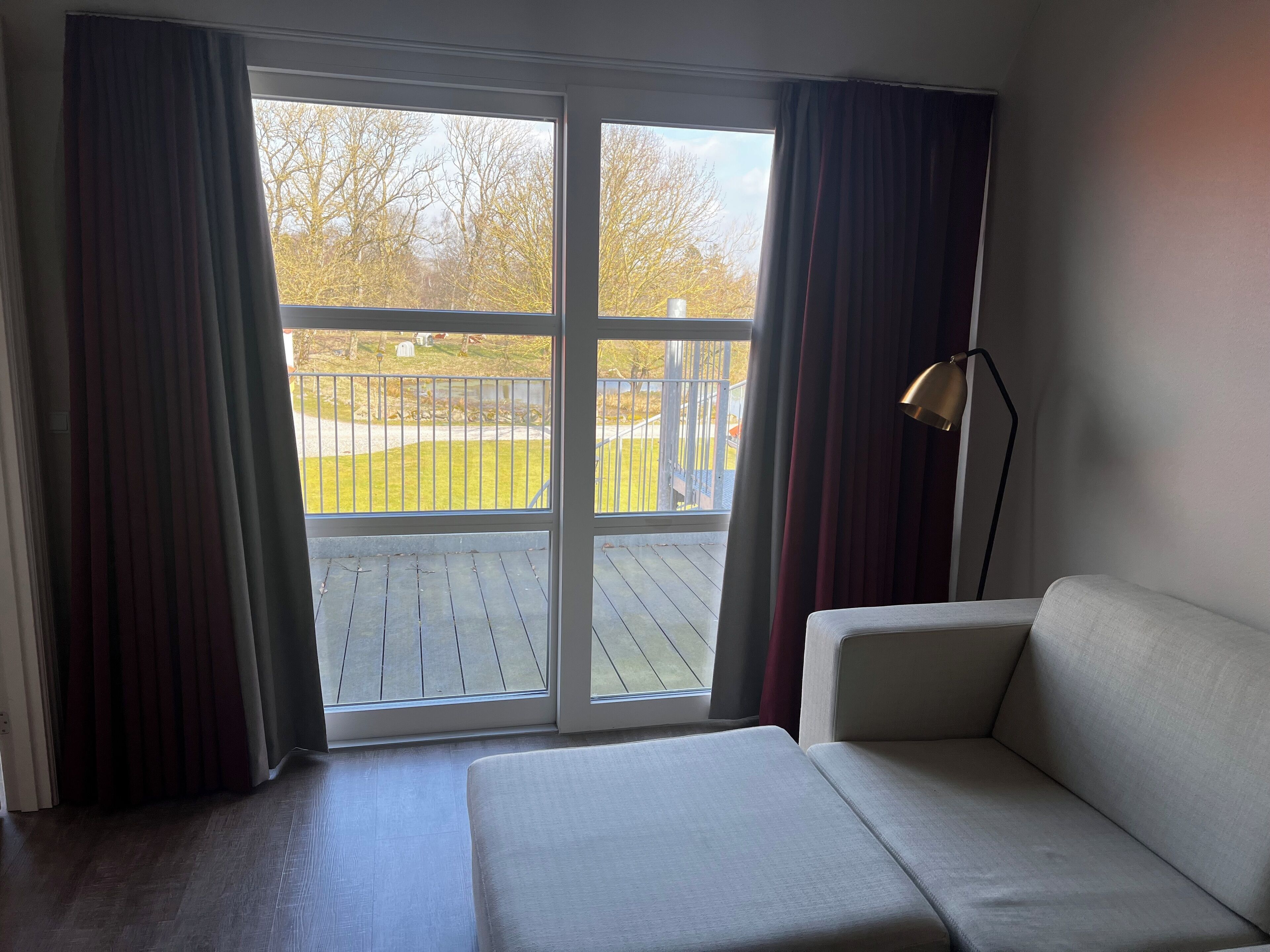 Quarto com sofá, luminária de chão e porta de vidro deslizante para um deck externo.