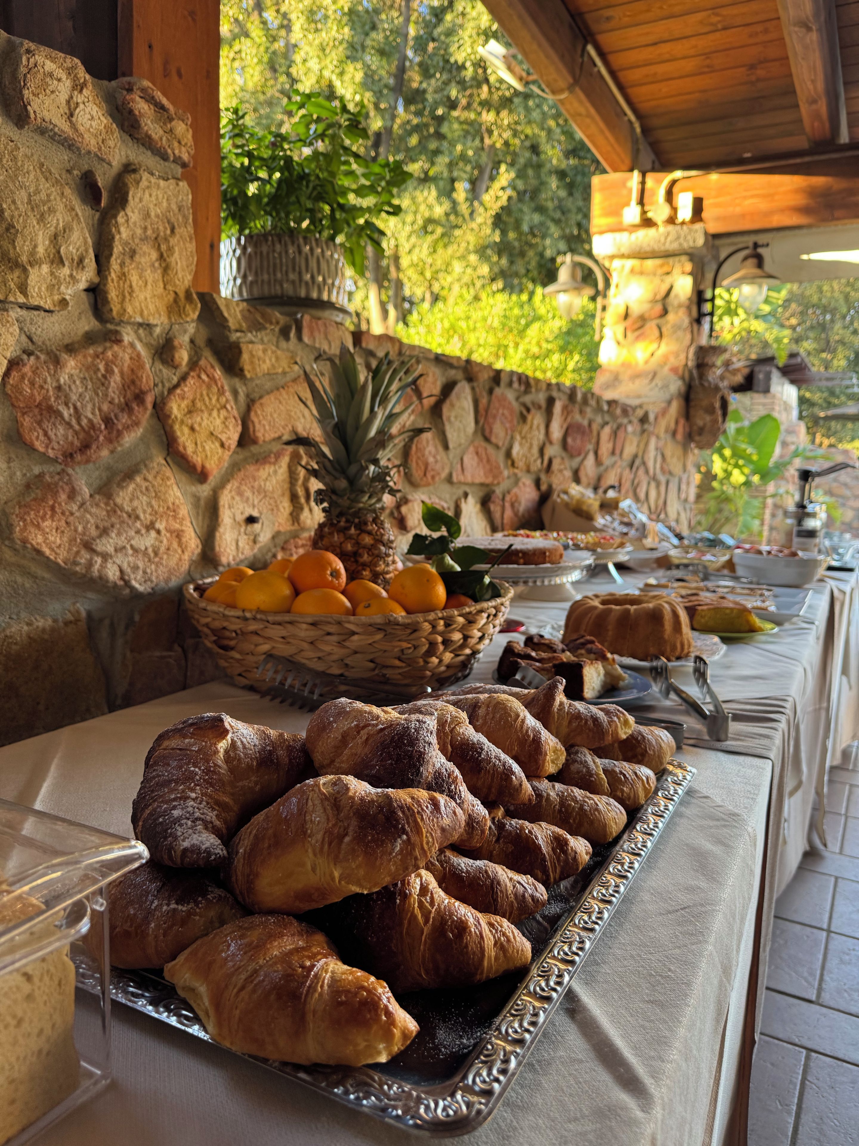 Mesa de buffet com doces, frutas e um fundo de parede de pedra.