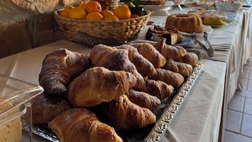 Mesa de buffet com doces, frutas e um fundo de parede de pedra.