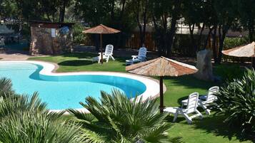 Piscina rodeada por cadeiras de banho brancas e uma estrutura de pedra.