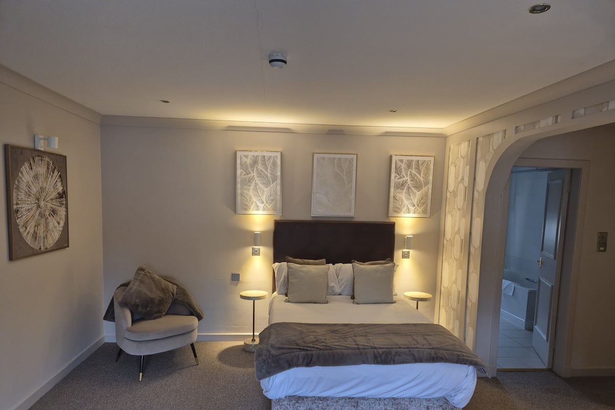 Quarto com cama, uma cadeira e três luminárias na parede.