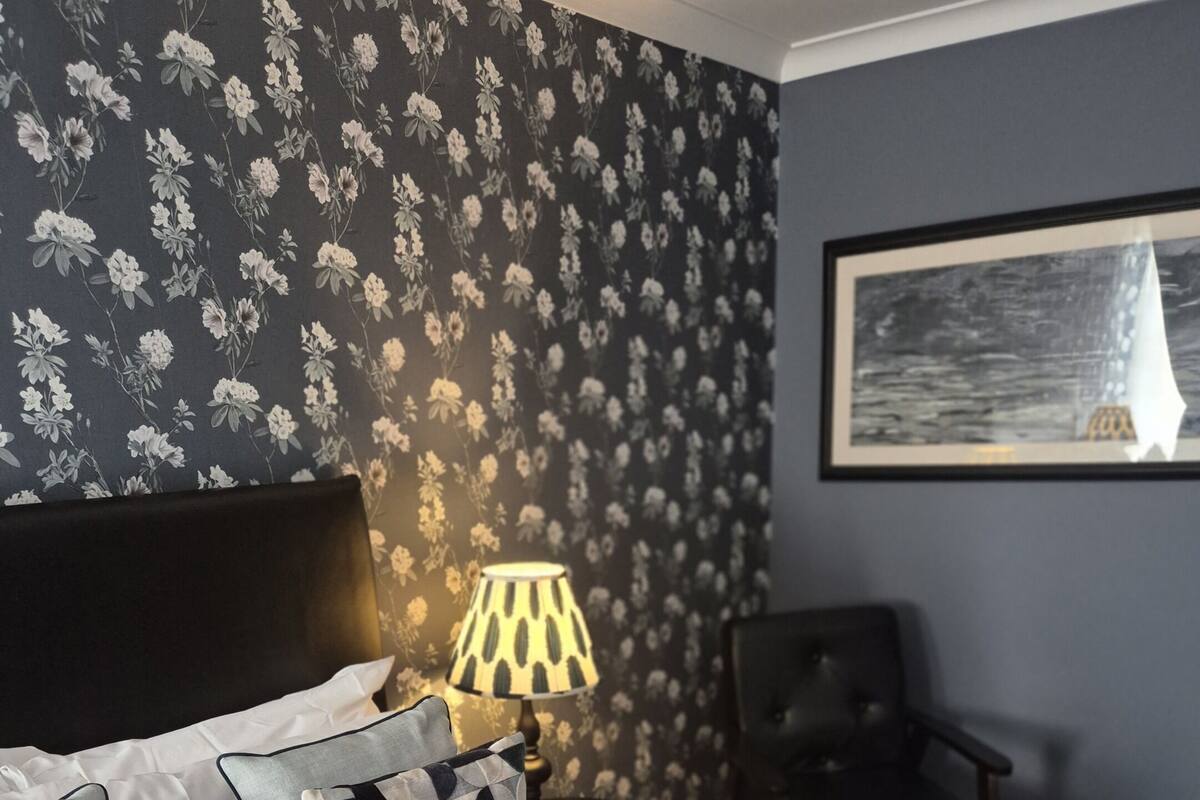 Quarto de hotel com uma cama grande, uma cadeira, um abajur e um quadro na parede.