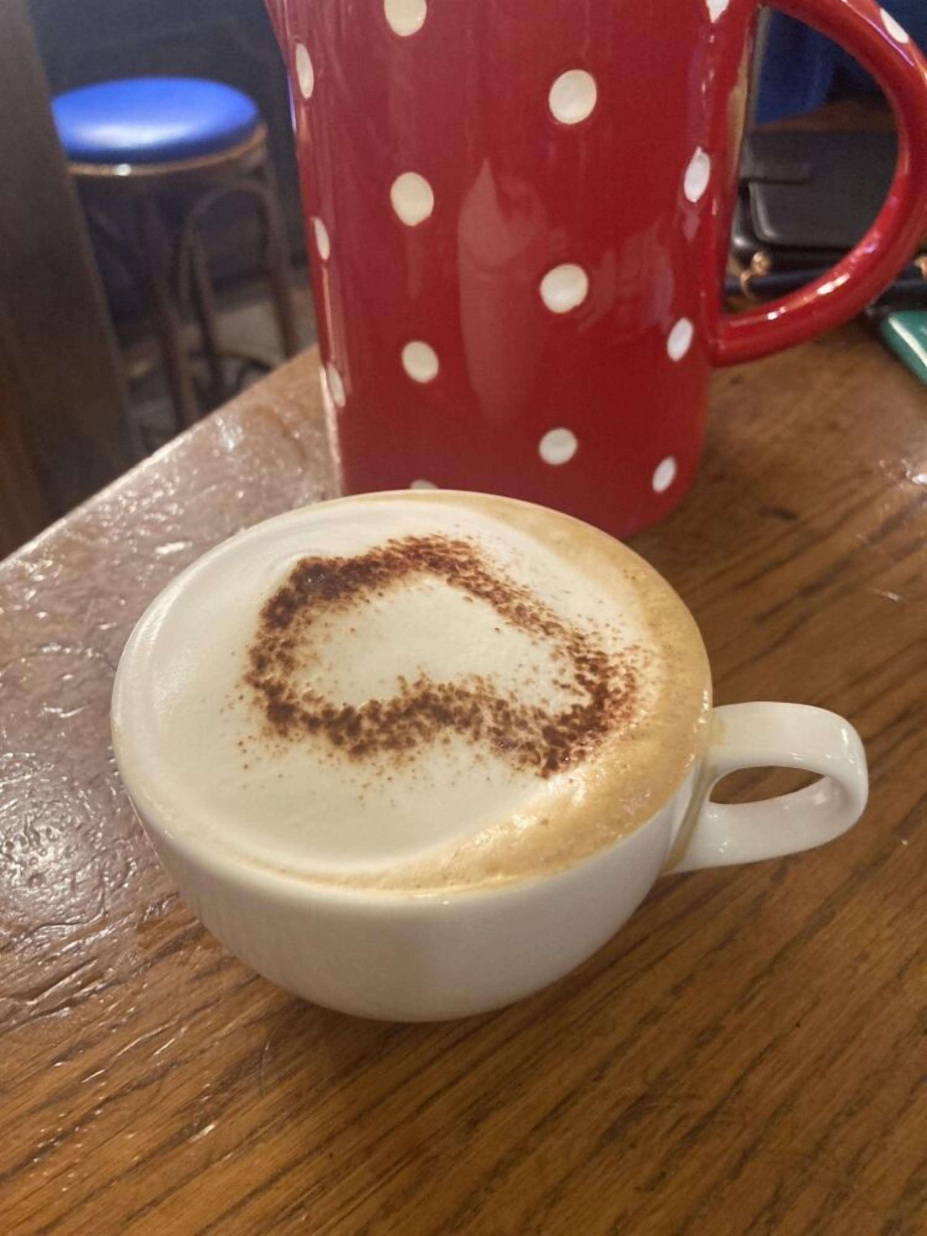 Uma chávena branca com arte latte sobre uma mesa de madeira.