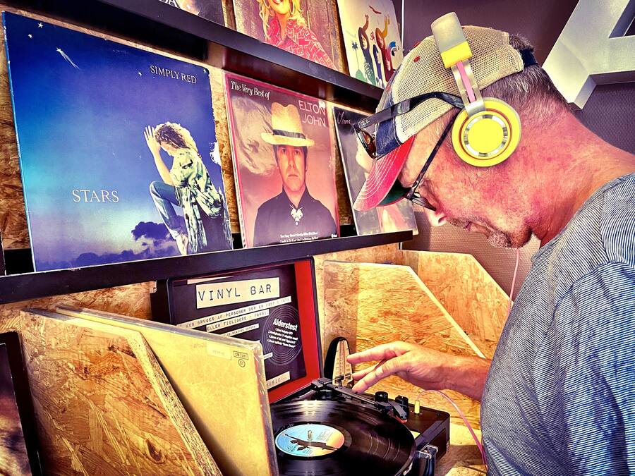 Um toca-discos de vinil com um disco em cima, rodeado por discos de vinil e capas de álbuns em prateleiras.