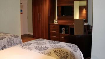 Quarto de hotel com uma cama, uma escrivaninha com cadeira, um guarda-roupa e uma televisão.