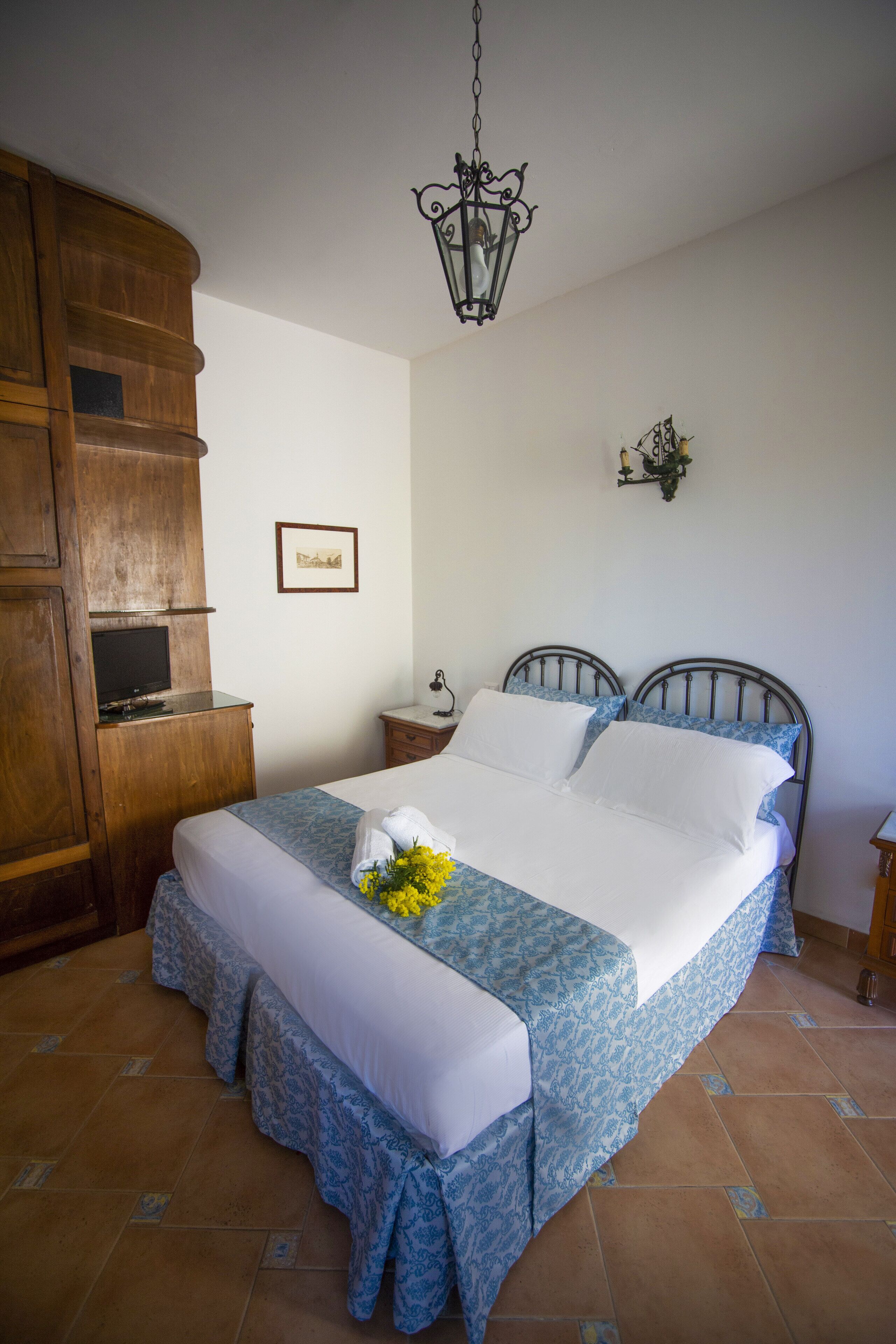 Quarto com cama, guarda-roupa de madeira, televisão, mesa de cabeceira e luminária na parede.