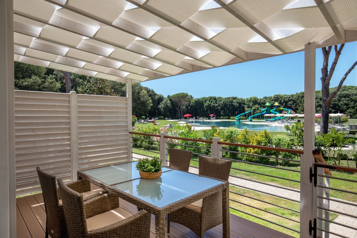 Área externa coberta com mesa e cadeiras, com vista para uma piscina e parque aquático.