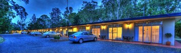 Um motel com uma fileira de quartos, cada um com porta e janelas, e uma área externa coberta com mesas e cadeiras.