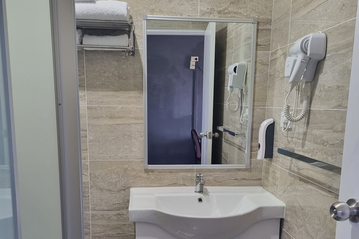 Casa de banho com lavatório branco, espelho, secador de cabelo e barra para toalhas.