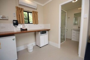 Quarto de hotel compacto com cozinha compacta, mini-geladeira, micro-ondas, lixeira e área de chuveiro.