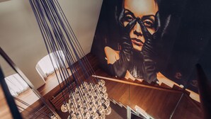 Quarto com uma pintura grande de uma pessoa, escada de madeira e luminária pendente.