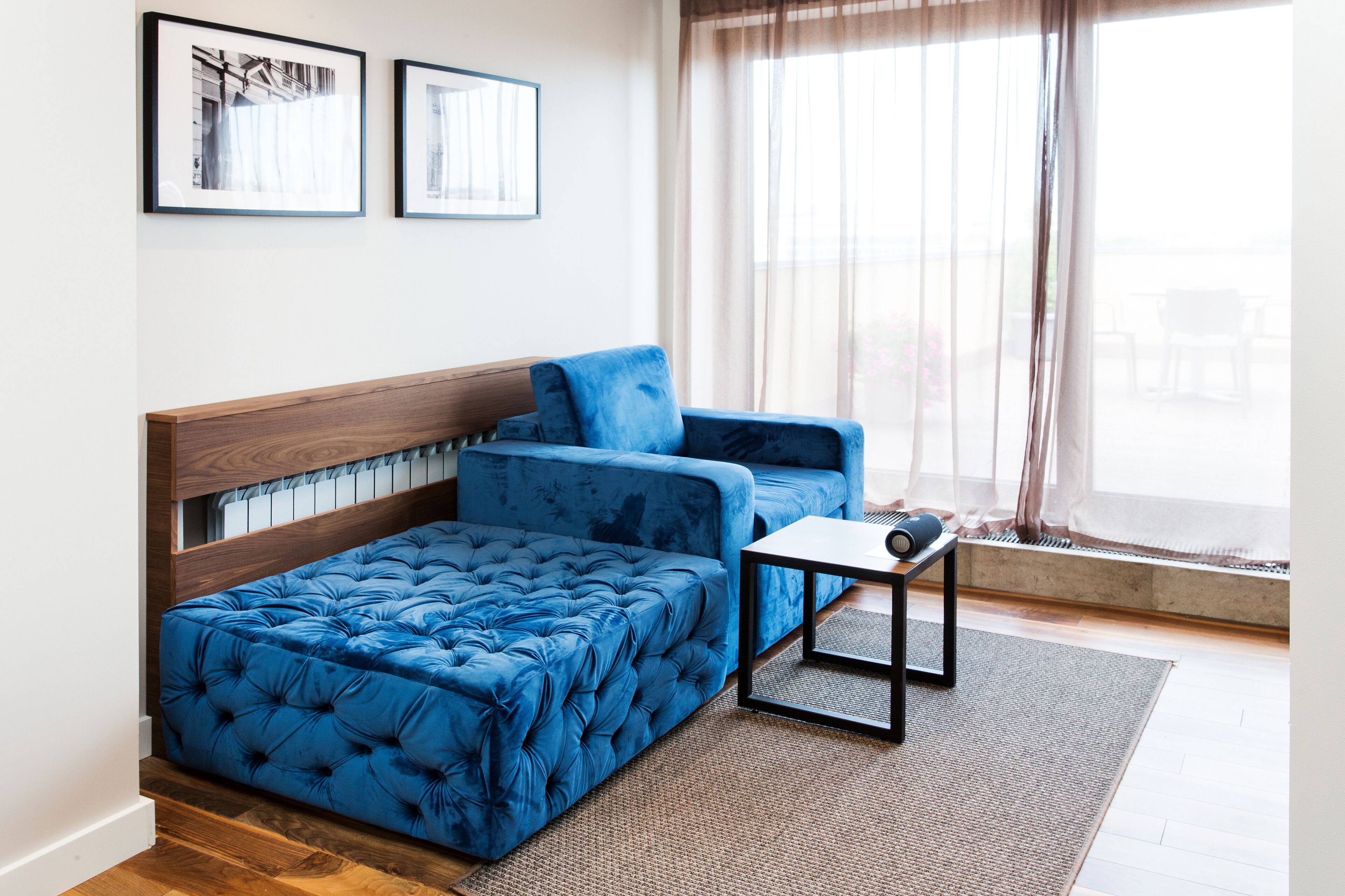Quarto moderno com um sofá azul estofado, uma cabeceira de madeira e uma pequena mesa.