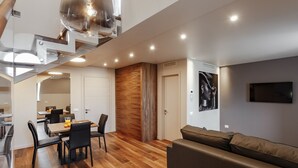 Uma sala de estar moderna com piso de madeira, um sofá, uma mesa de jantar com cadeiras e uma cozinha ao fundo.