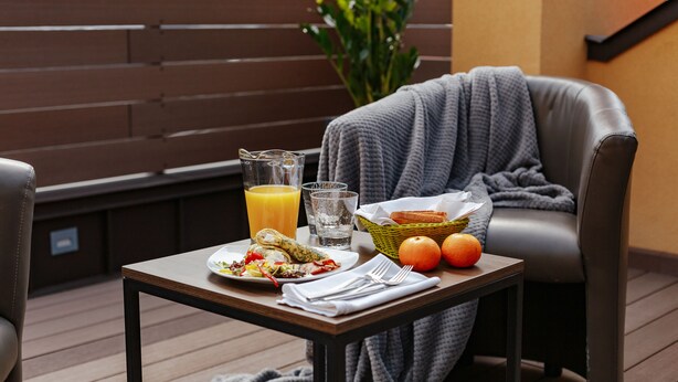 Uma mesa de café da manhã com um prato de comida, um copo de suco de laranja, um copo de água, uma cesta de pão e duas laranjas.