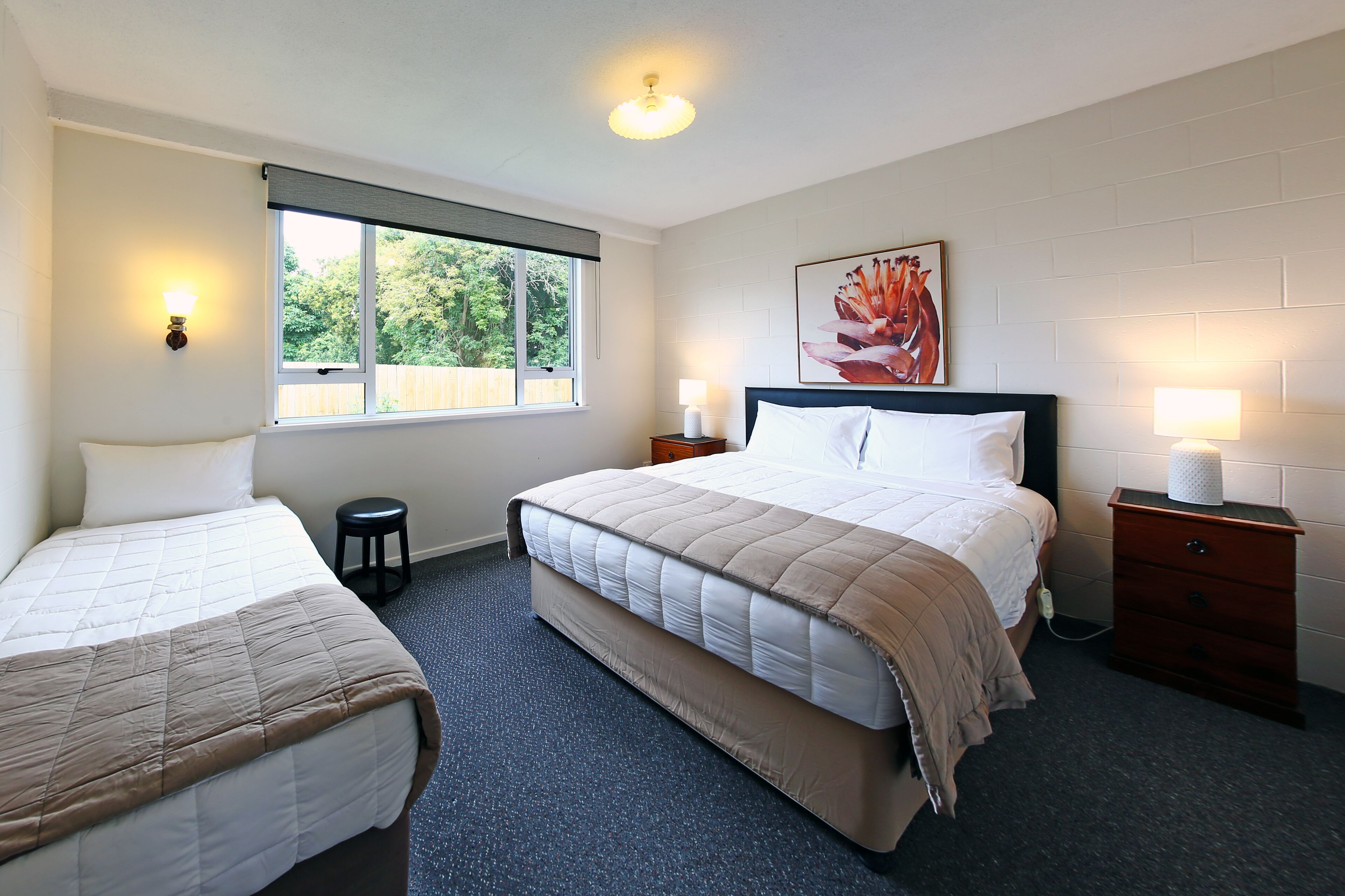 Quarto de hotel com duas camas, janela com vista para o verde, um quadro na parede e abajures.