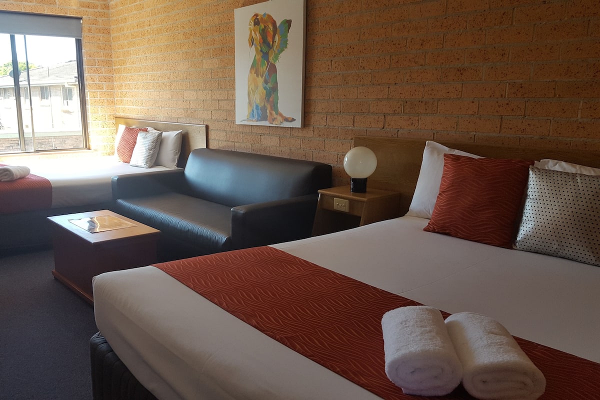 Quarto de hotel com uma cama grande, um sofá, uma mesa pequena e uma janela.