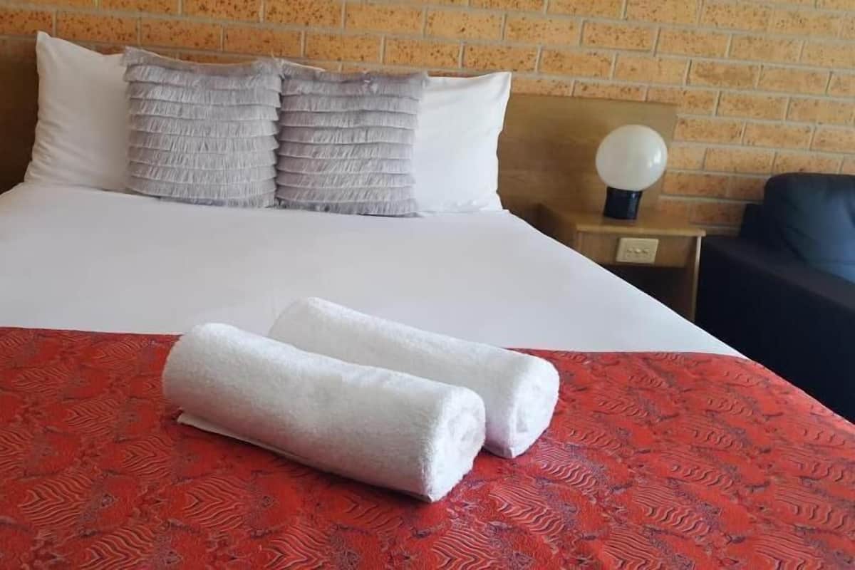 Quarto de hotel com cama, duas mesas de cabeceira e colcha vermelha estampada.